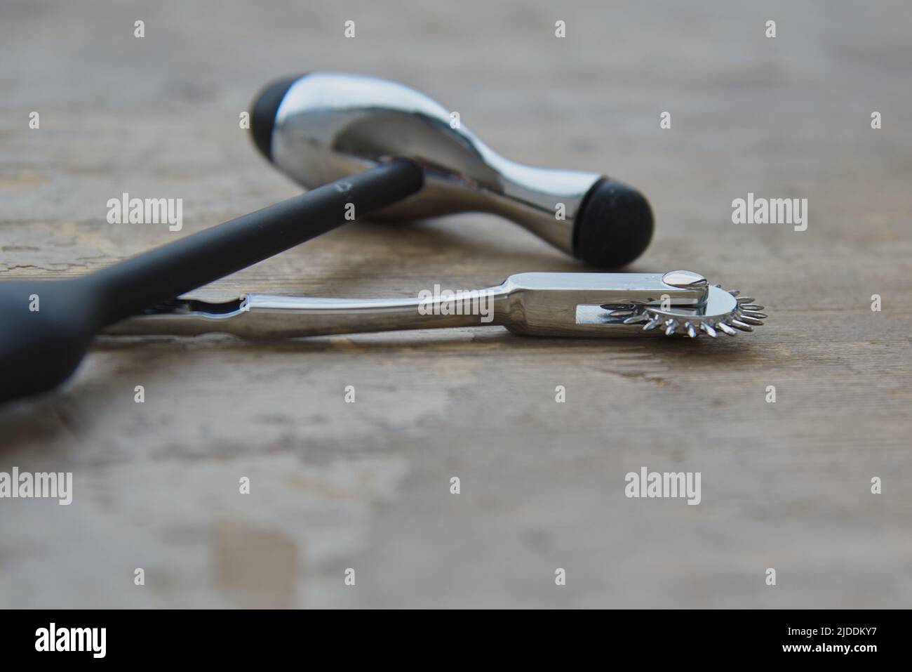 A medical reflex hammer and a Wartenberg wheel lie on a gray wooden ...