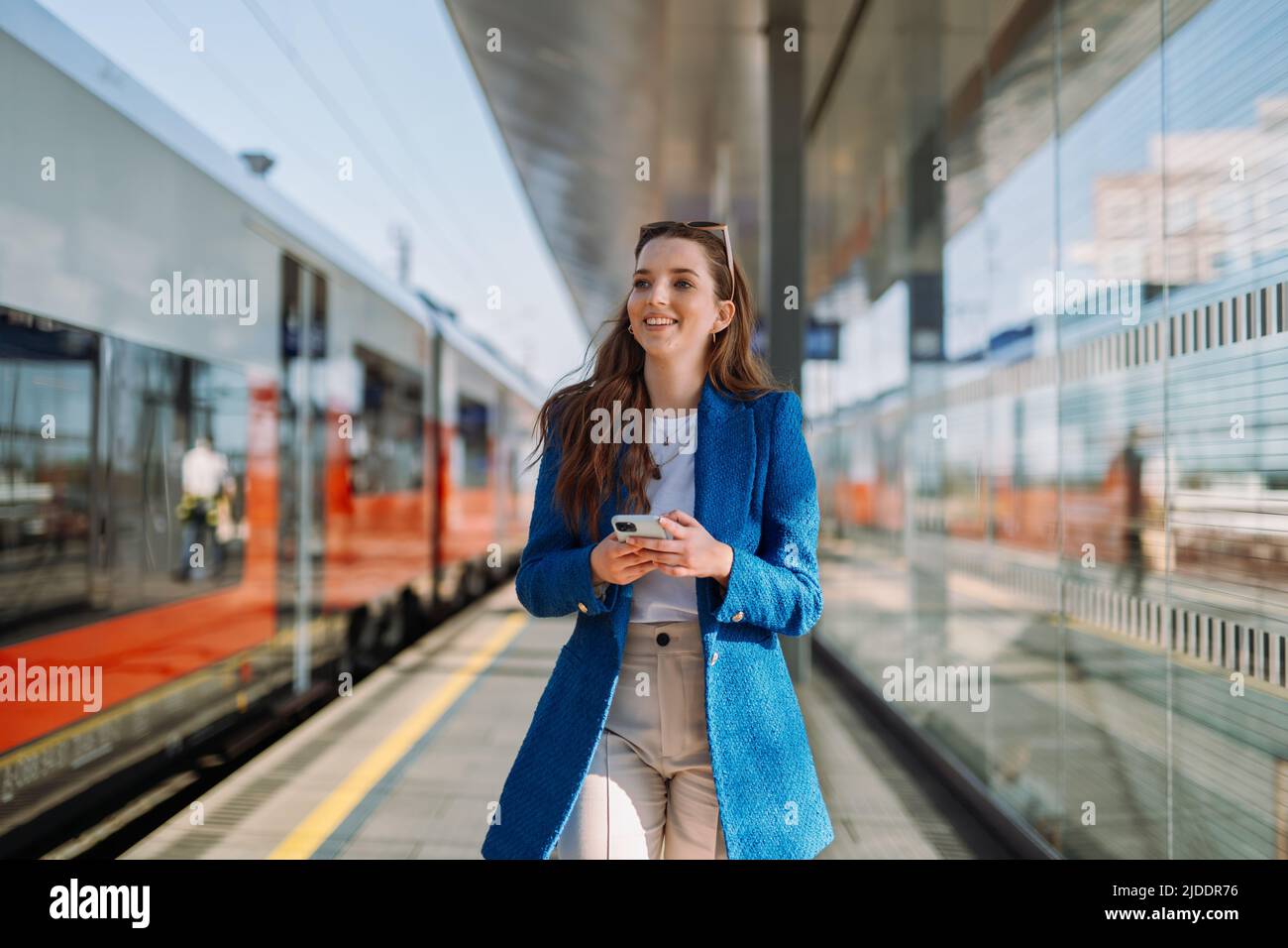 Young woman holding mobile in a train station. Commuting to work ...