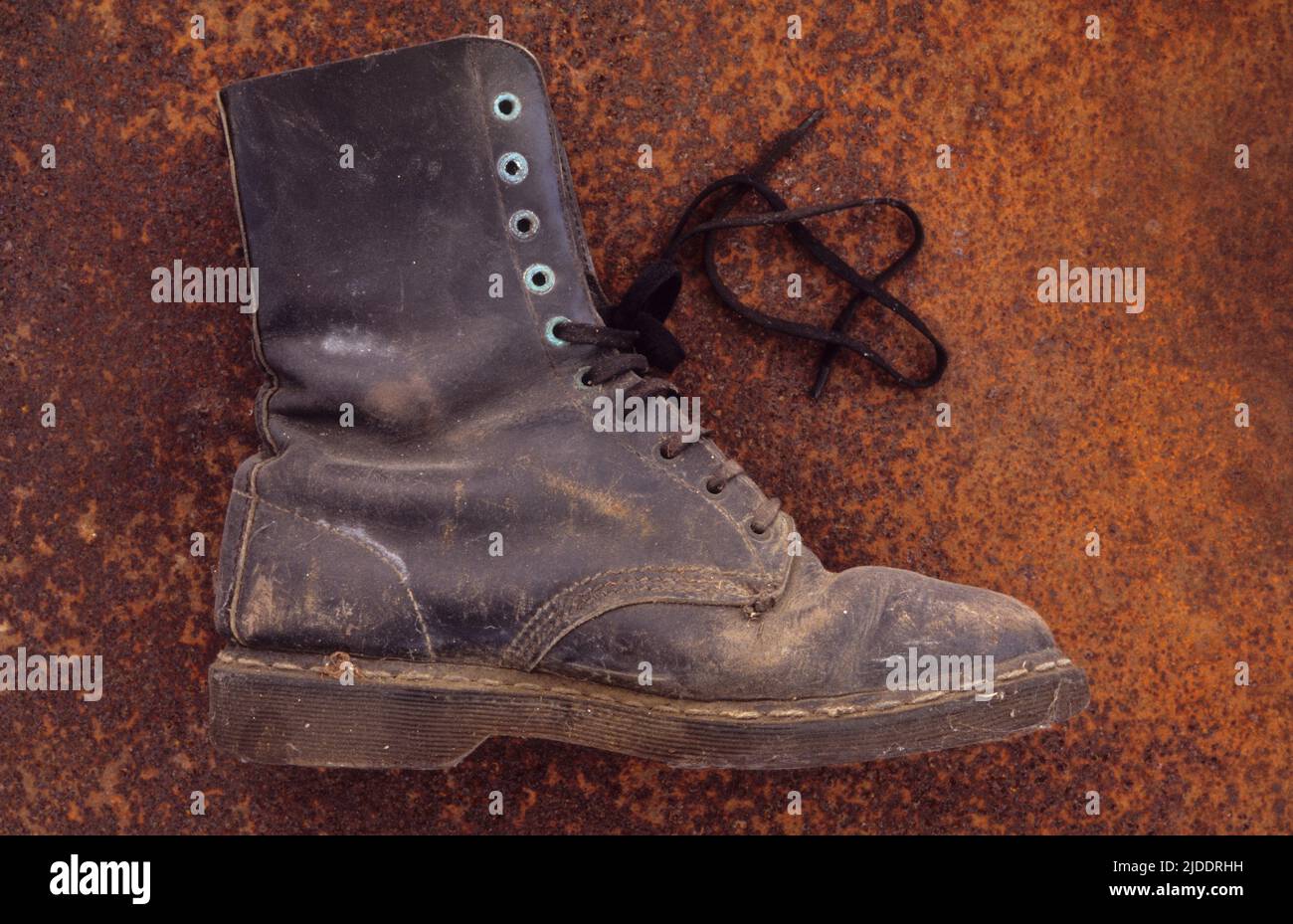 Well-worn black heavy-duty industrial working boot lying on rusty metal ...