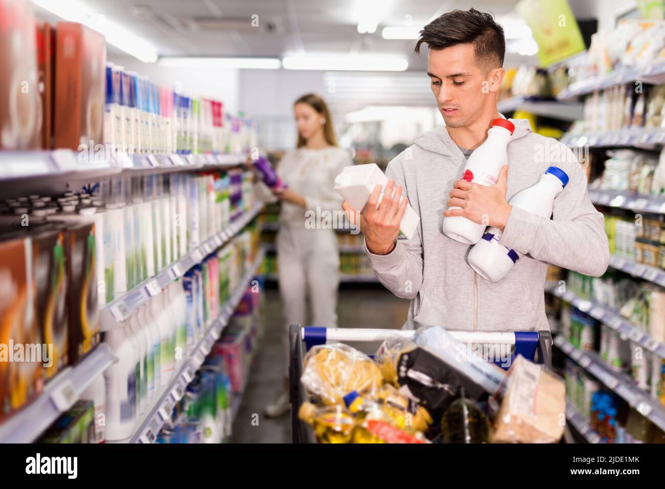 Young smiling male customer choosing milk and dairy products in ...