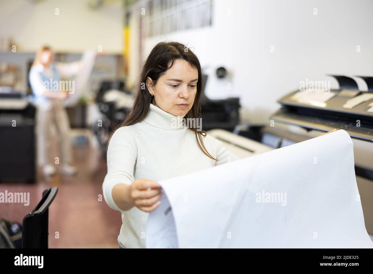 Woman checking large format paper after printing Stock Photo - Alamy