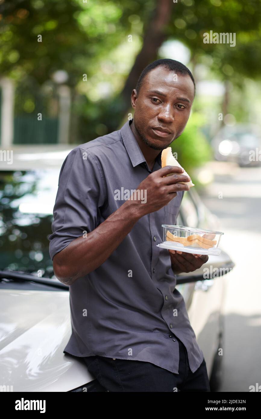Portrait of taxi driver leaning on car and eating sandwich for lunch ...