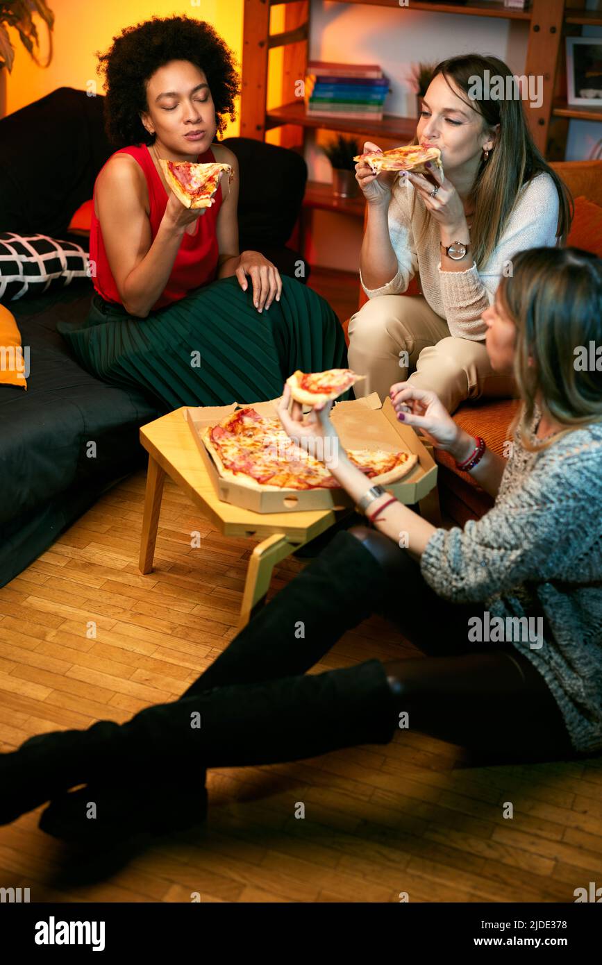 Happy multicultural female friends having party at home and eating ...