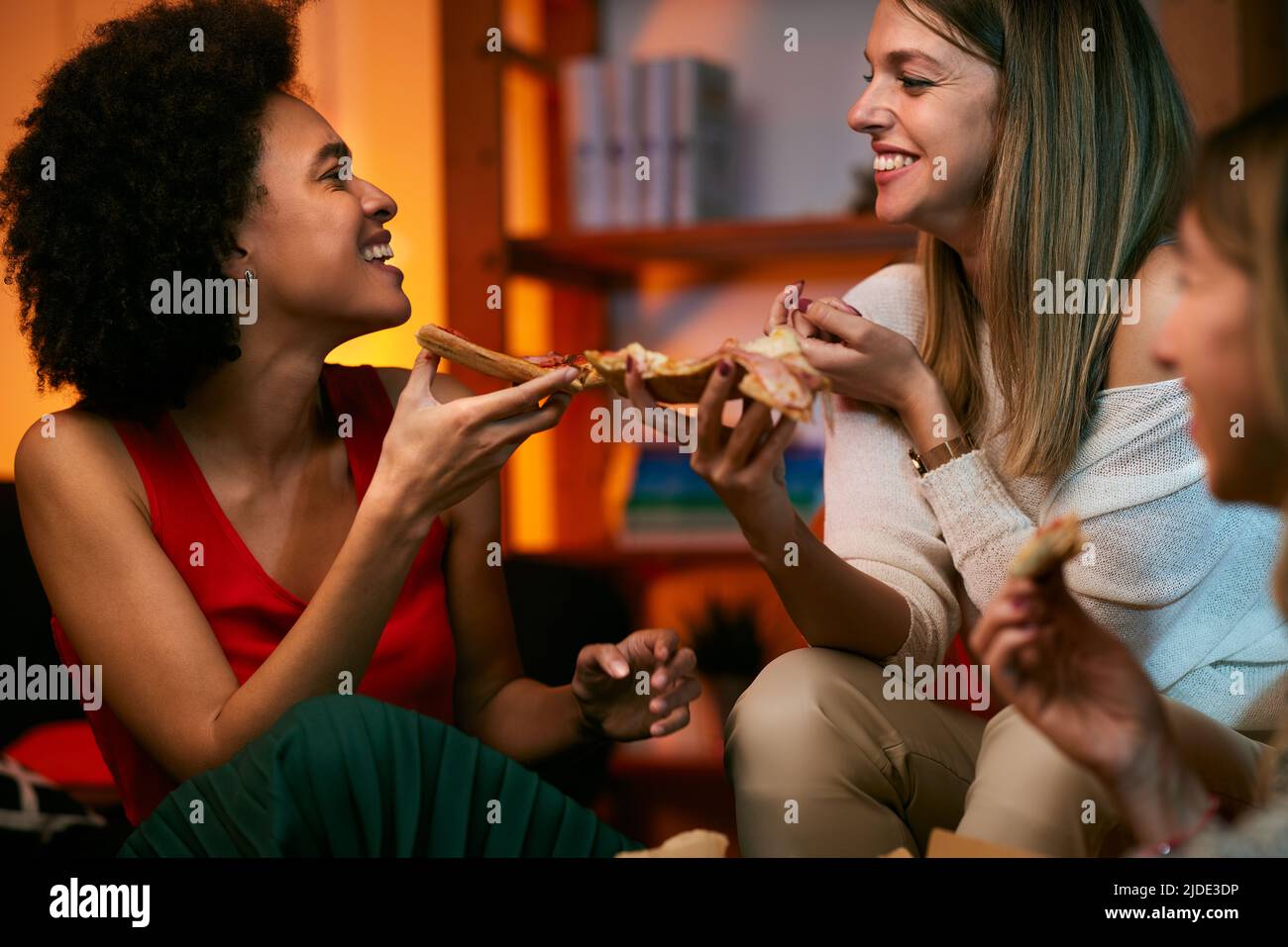 Happy multicultural female friends having party at home and eating ...