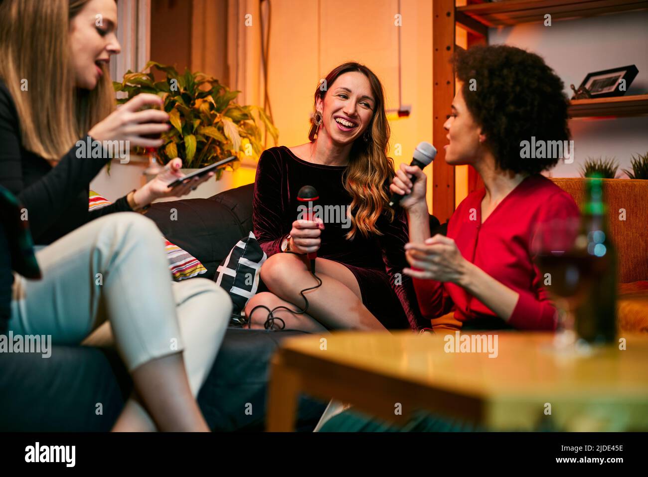A multicultural group of female friends sings karaoke while drinking ...
