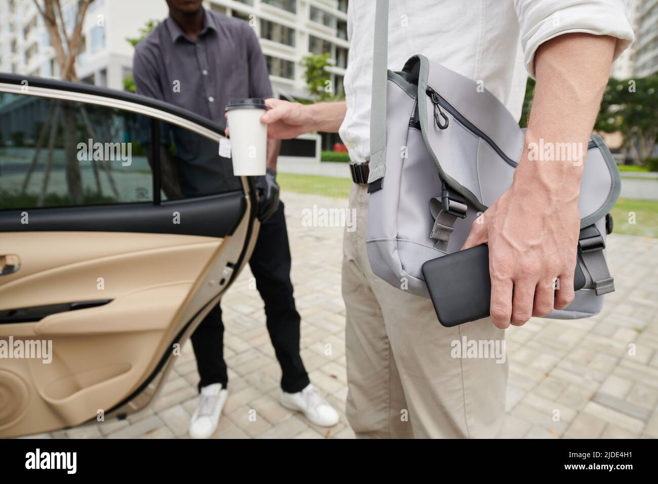 Taxi driver opening door for passenger with cup of tea, bag and ...