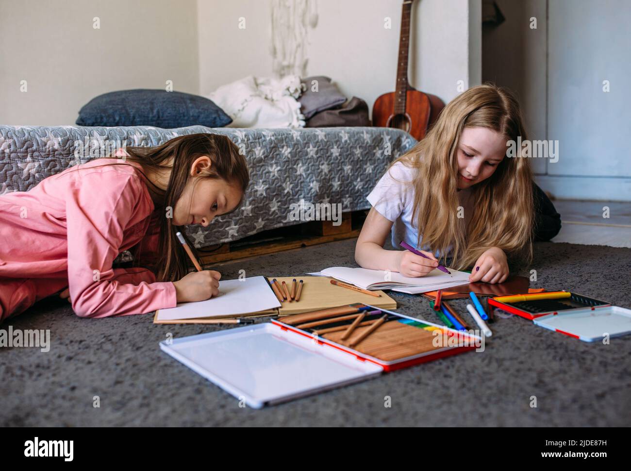 Two girls friends play at home, draw with pencils and felt-tip pens and ...