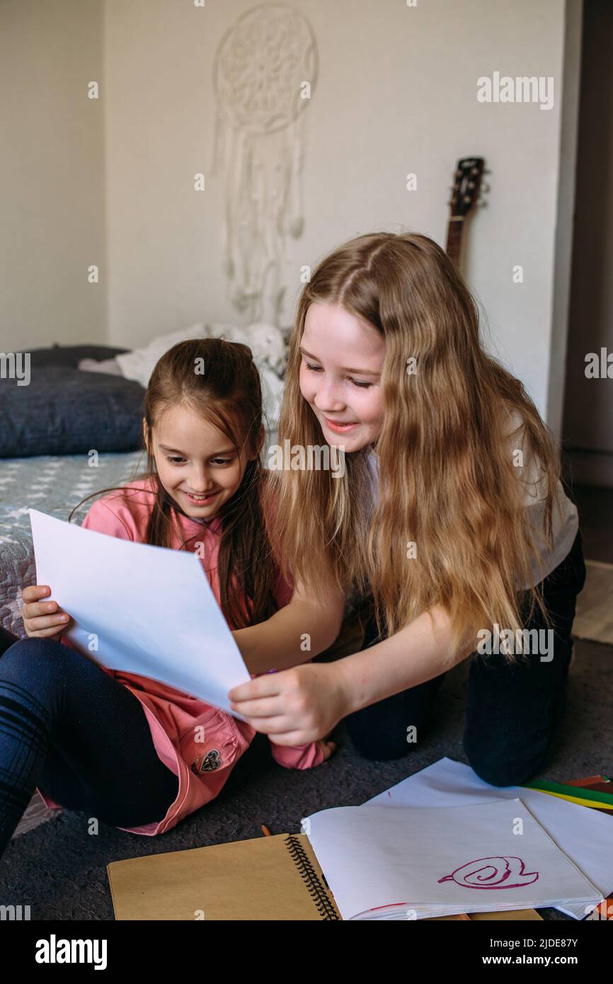 Two girls friends play at home, draw with pencils and felt-tip pens and ...