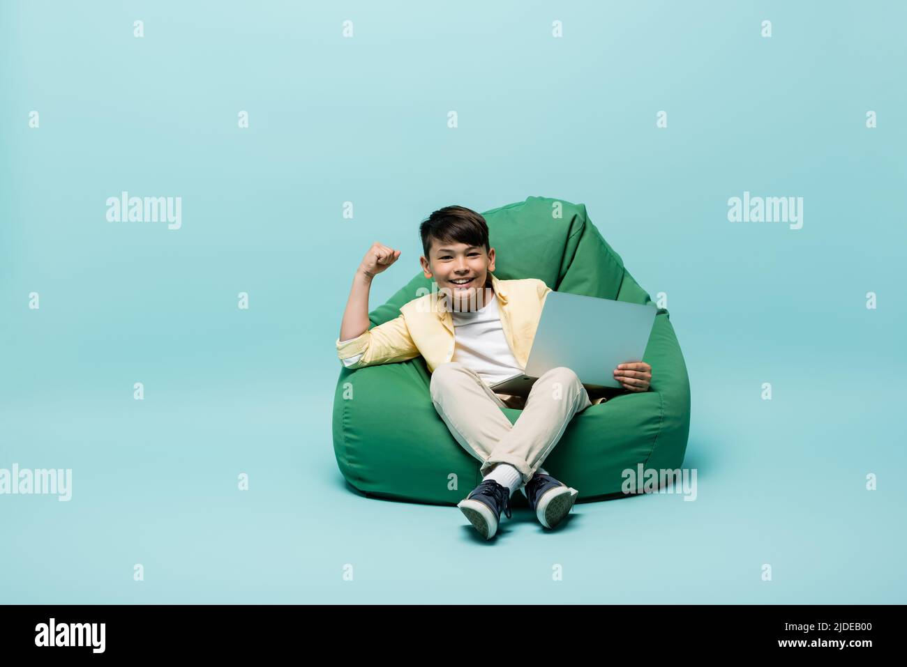 Smiling asian schoolkid showing yes gesture and holding laptop on ...