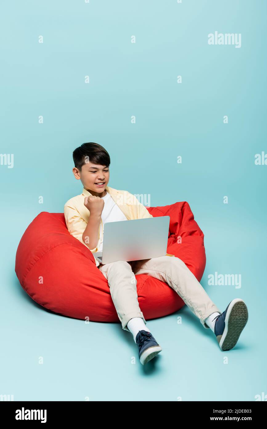 Excited asian schoolchild showing yes gesture while using laptop on ...