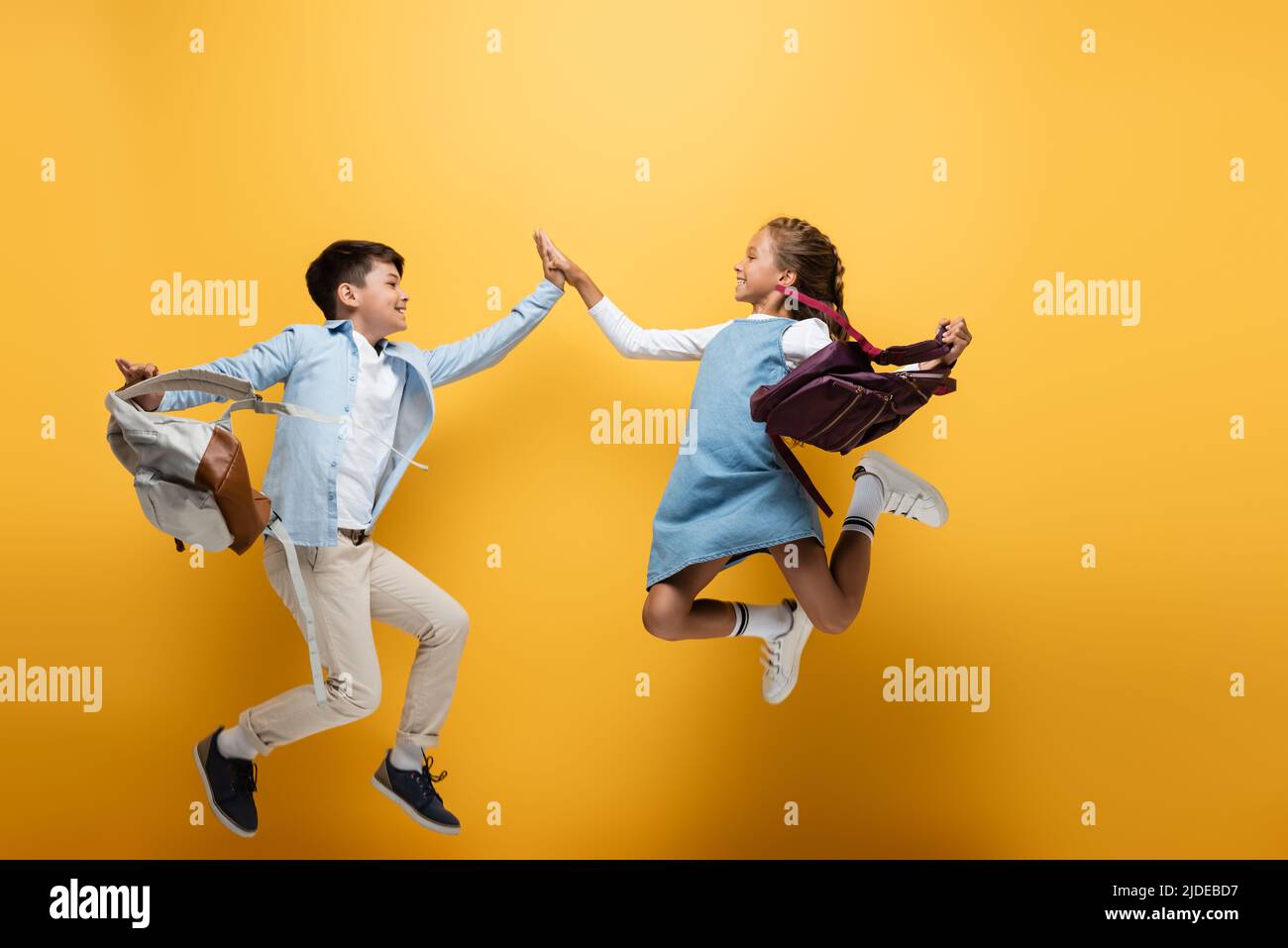 Side view of multiethnic schoolkids with backpacks giving high five ...