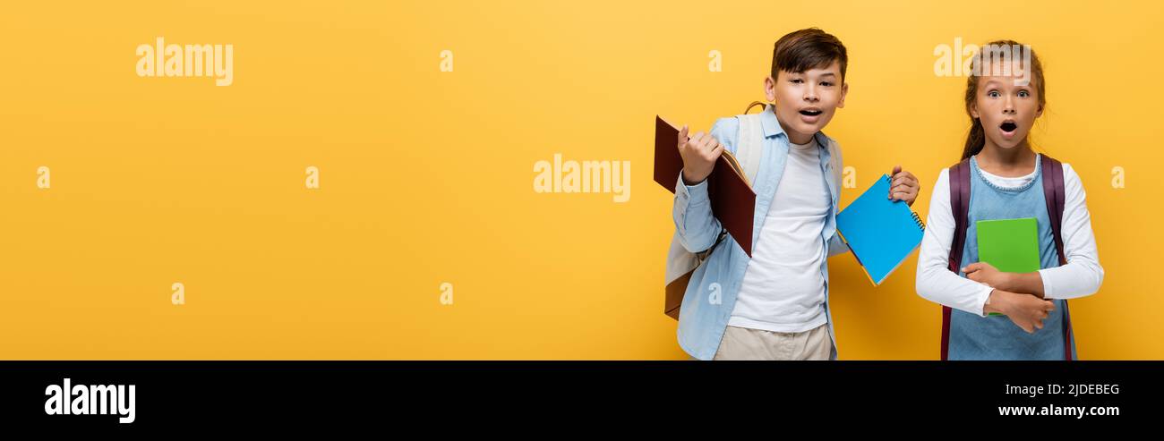 Shocked interracial classmates holding books and looking at camera on ...