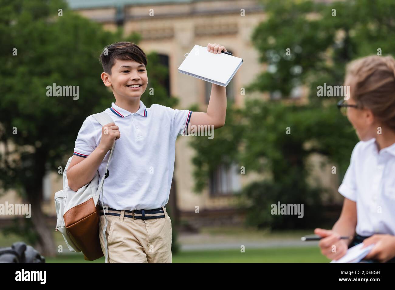 Asian schoolboy holding book near blurred classmate in park Stock Photo ...