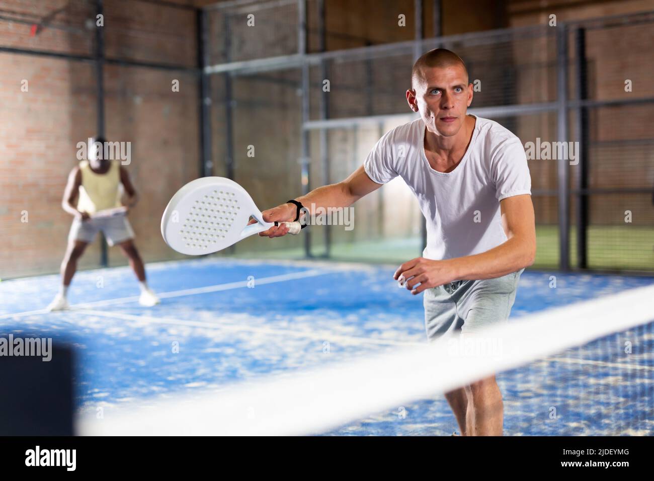 Padel player playing padel in a padel court indoor behind net Stock ...