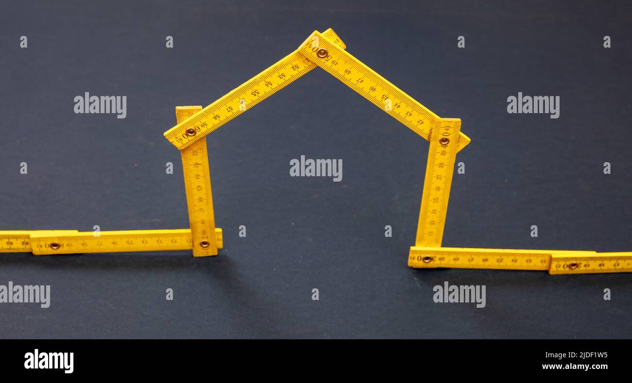 Home repair. House shape yellow wooden measure, gray black background ...