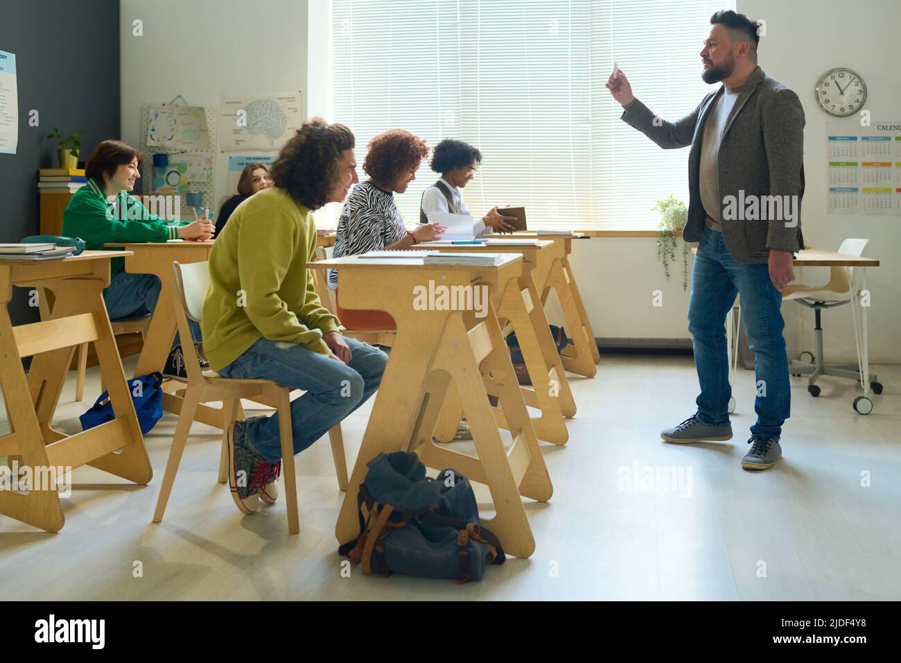 Group of students sitting by desks in classroom and listening to ...