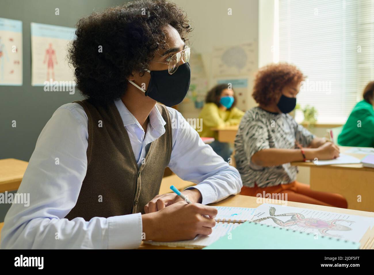 African American guy in black protective maks listening to teacher at ...