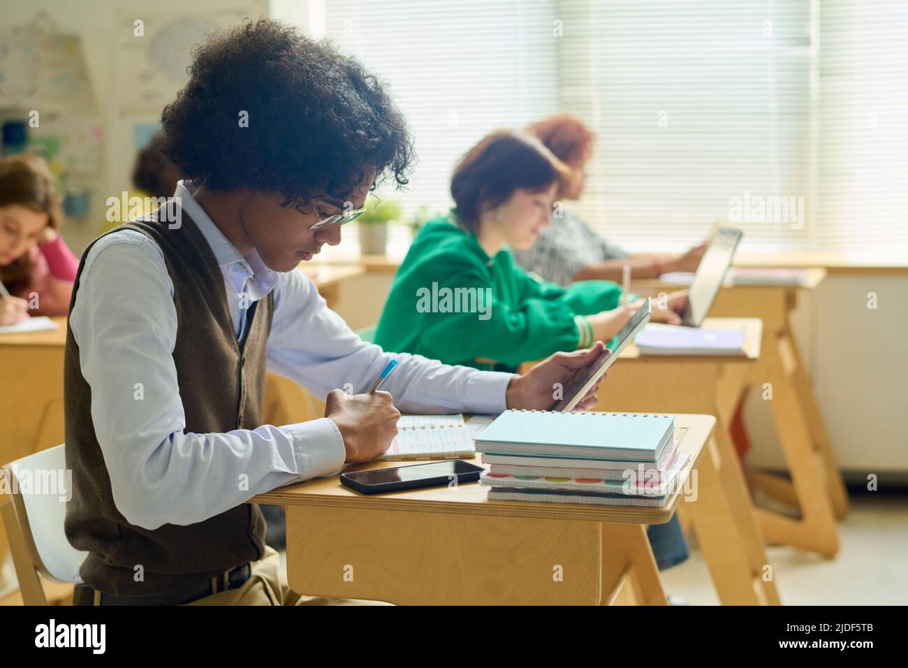 Side view of teenage guy with tablet carrying out individual assignment ...