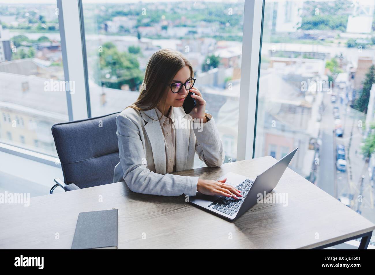 A woman manager in glasses sits at a laptop in an office with a ...