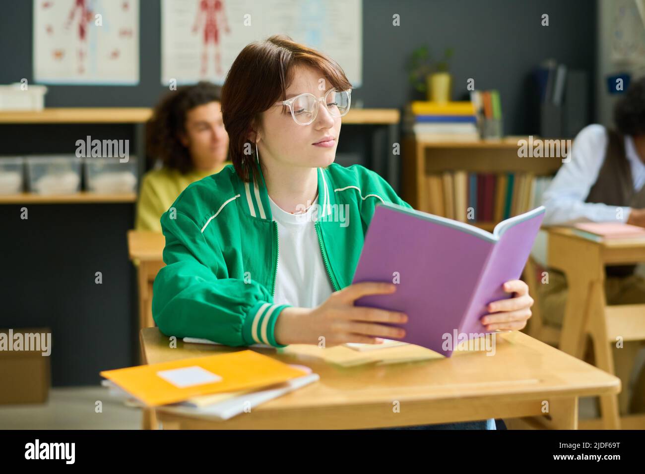 Serious teenage female student looking through her notes in copybook ...