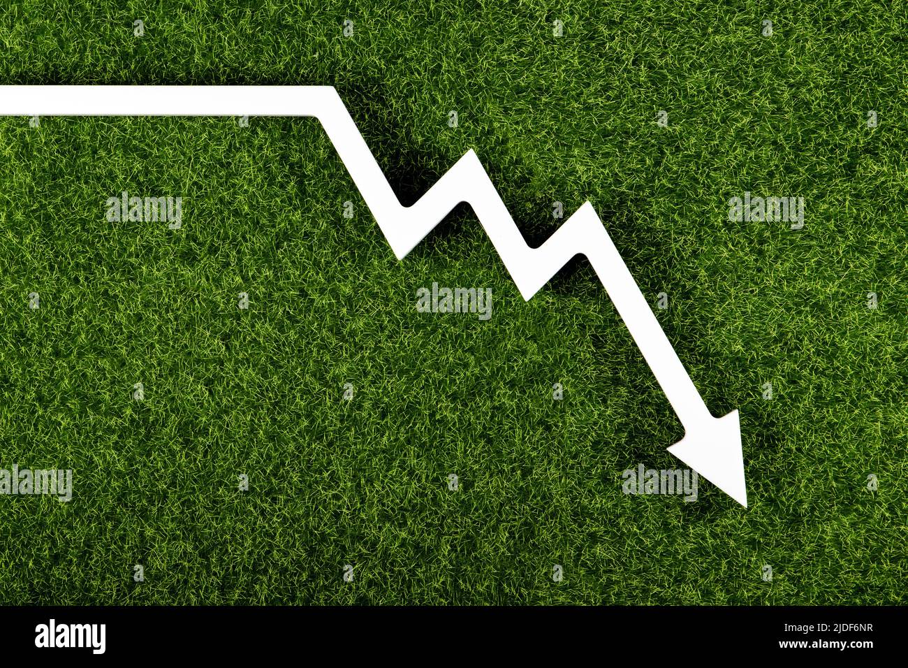 White chart arrow on green grass pointing down. Business loss symbol ...