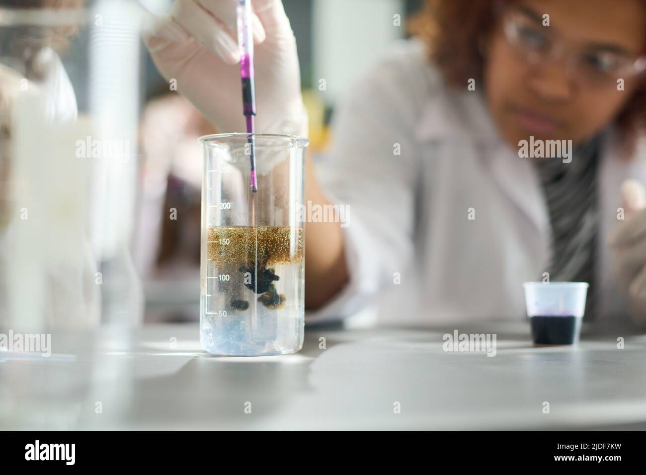 Female highschool student or researcher adding several drops of purple ...