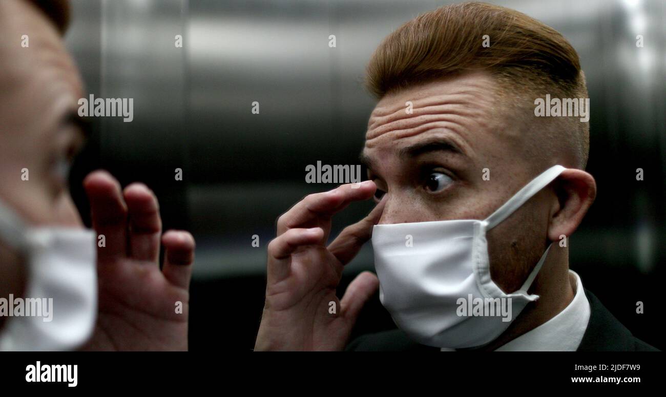 Business man wearing covid-19 face mask looking at himself in elevator ...