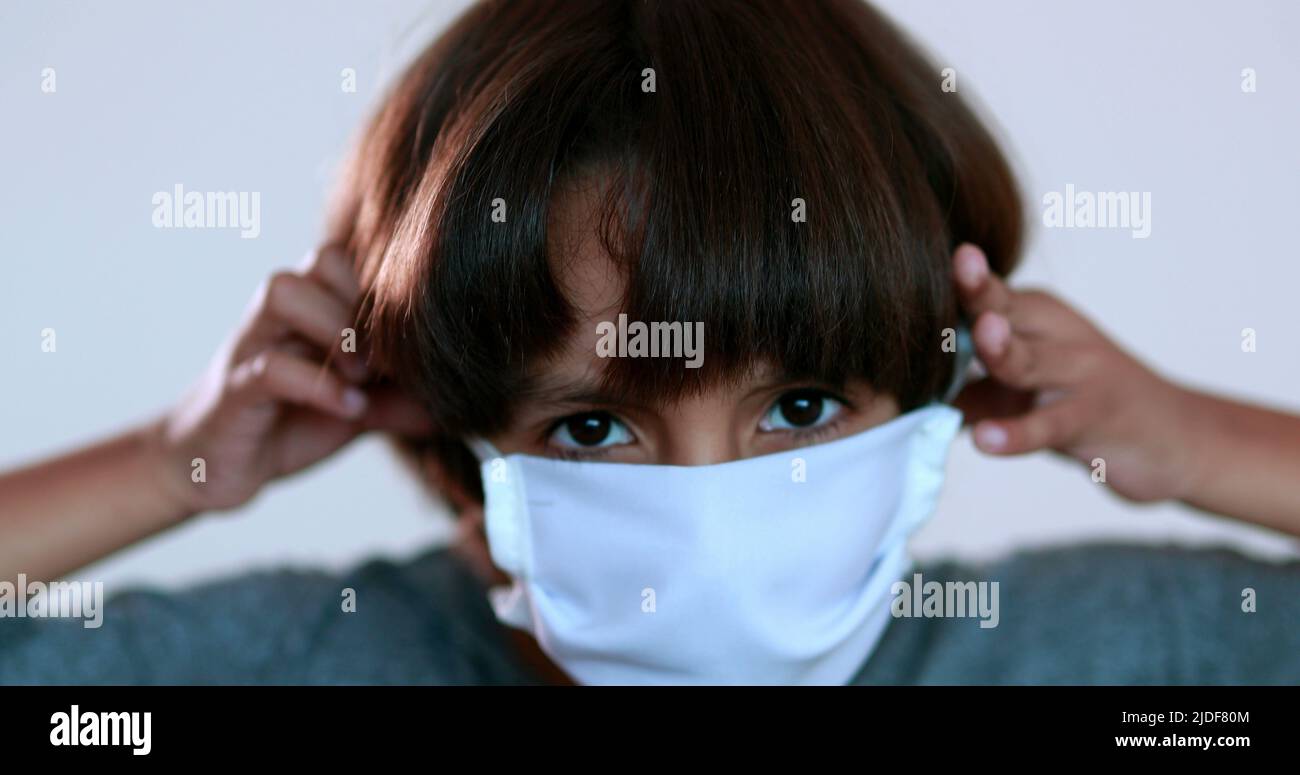 Child putting on covid-19 mask against pandemic prevention. Mixed race kid wearing surgical mask ...