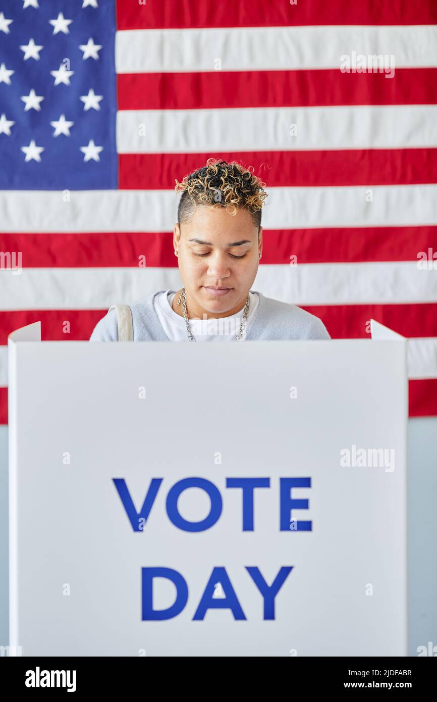 Vertical portrait of young black woman standing in voting booth on ...