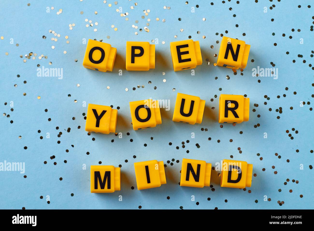 Flat lay yellow letters saying open your mind. Many sequins on blue ...