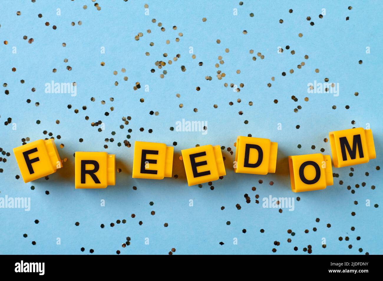 Yellow letter cube blocks saying word freedom. Many sequins on blue ...