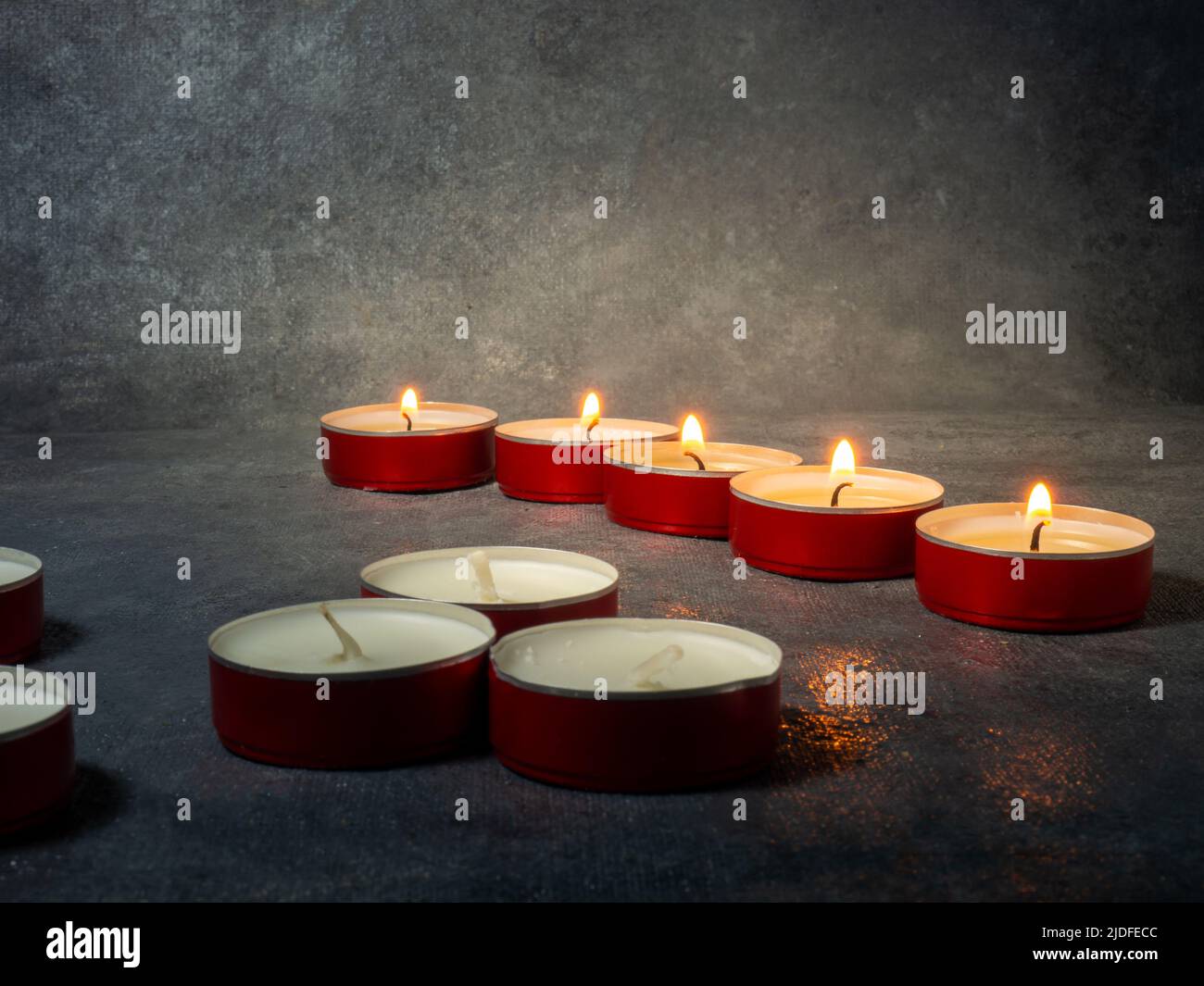 Short candles are burning on a dark surface. Lots of small candles. Not ...