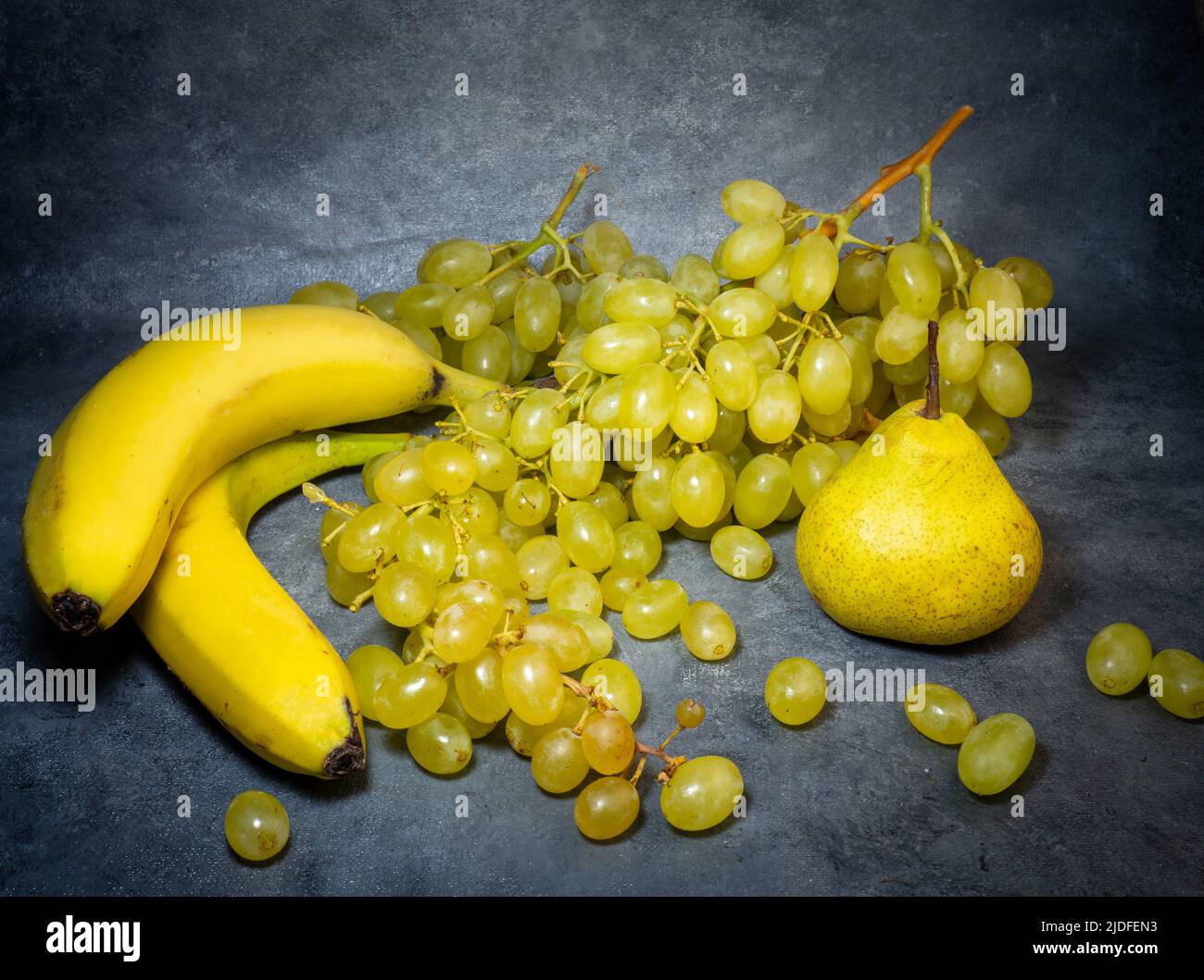 A large bunch of grapes with bananas and pears on a black background ...