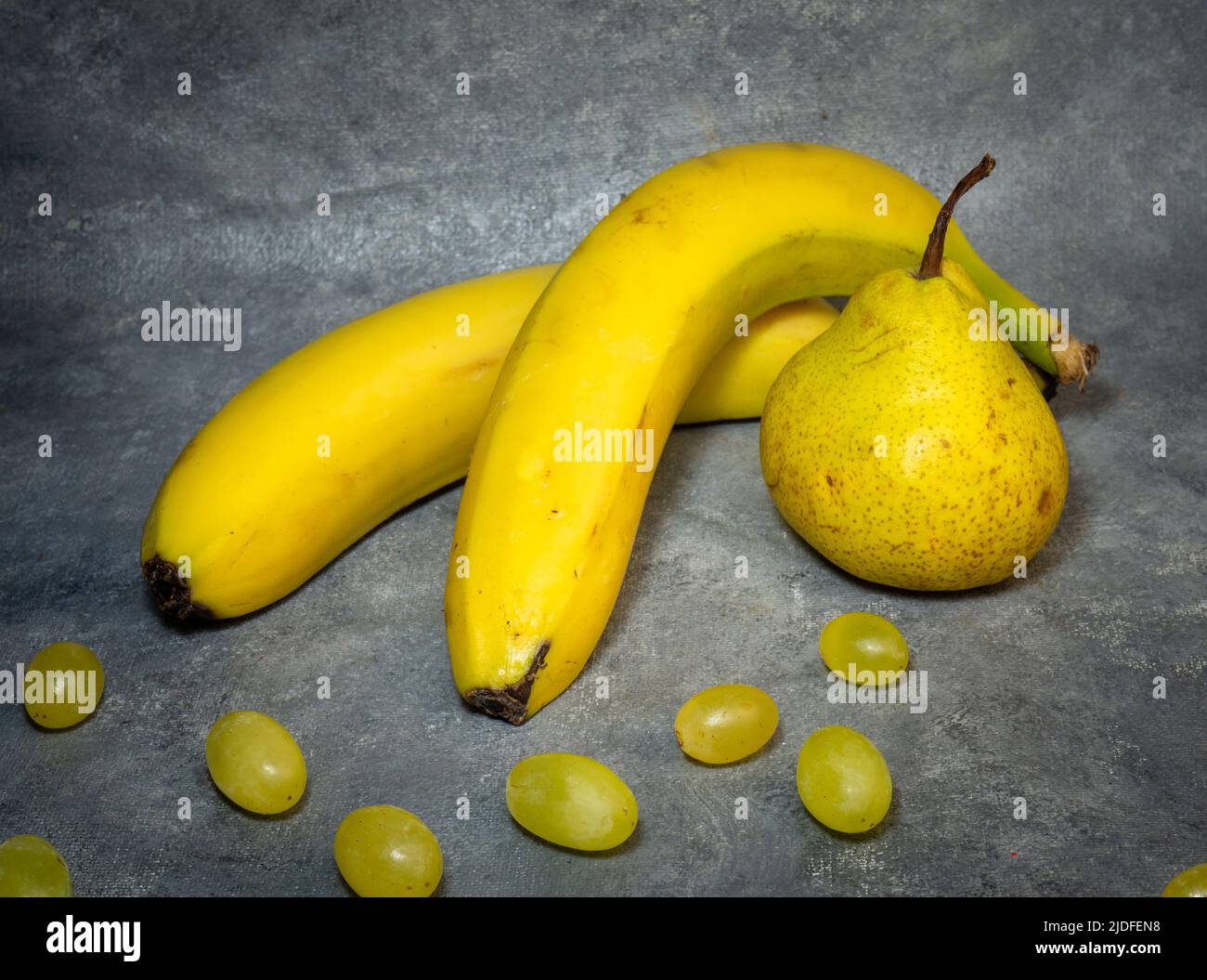 pear, two bananas and a scattering of green grapes on a black ...