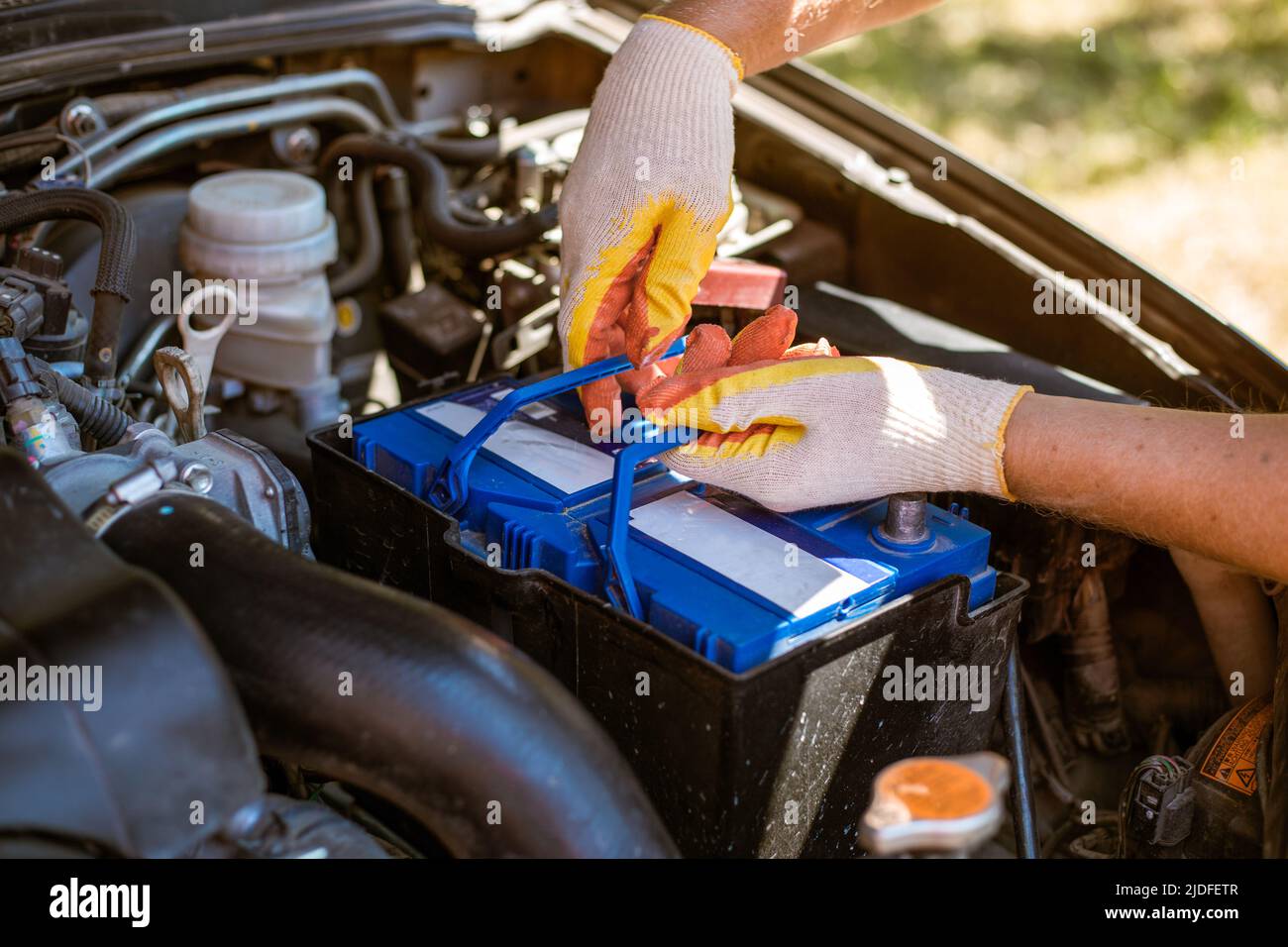 A man removes a battery from under the hood of a car. Battery ...
