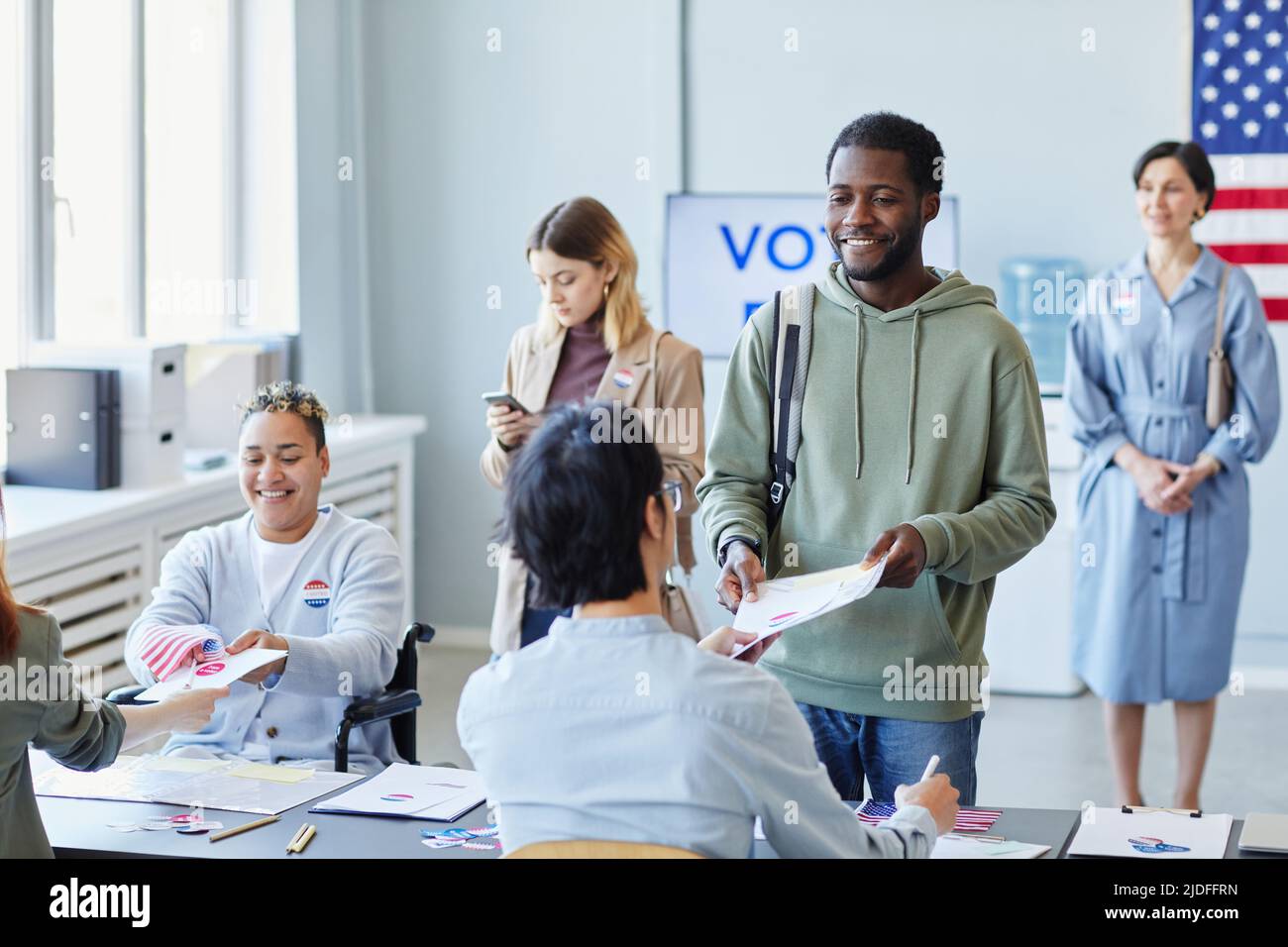 Diverse group of people voting in line and receiving ballot forms focus ...