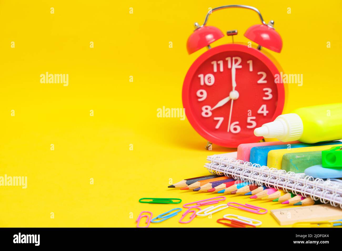 Red alarm clock and school supplies yellow background.Preparing child ...