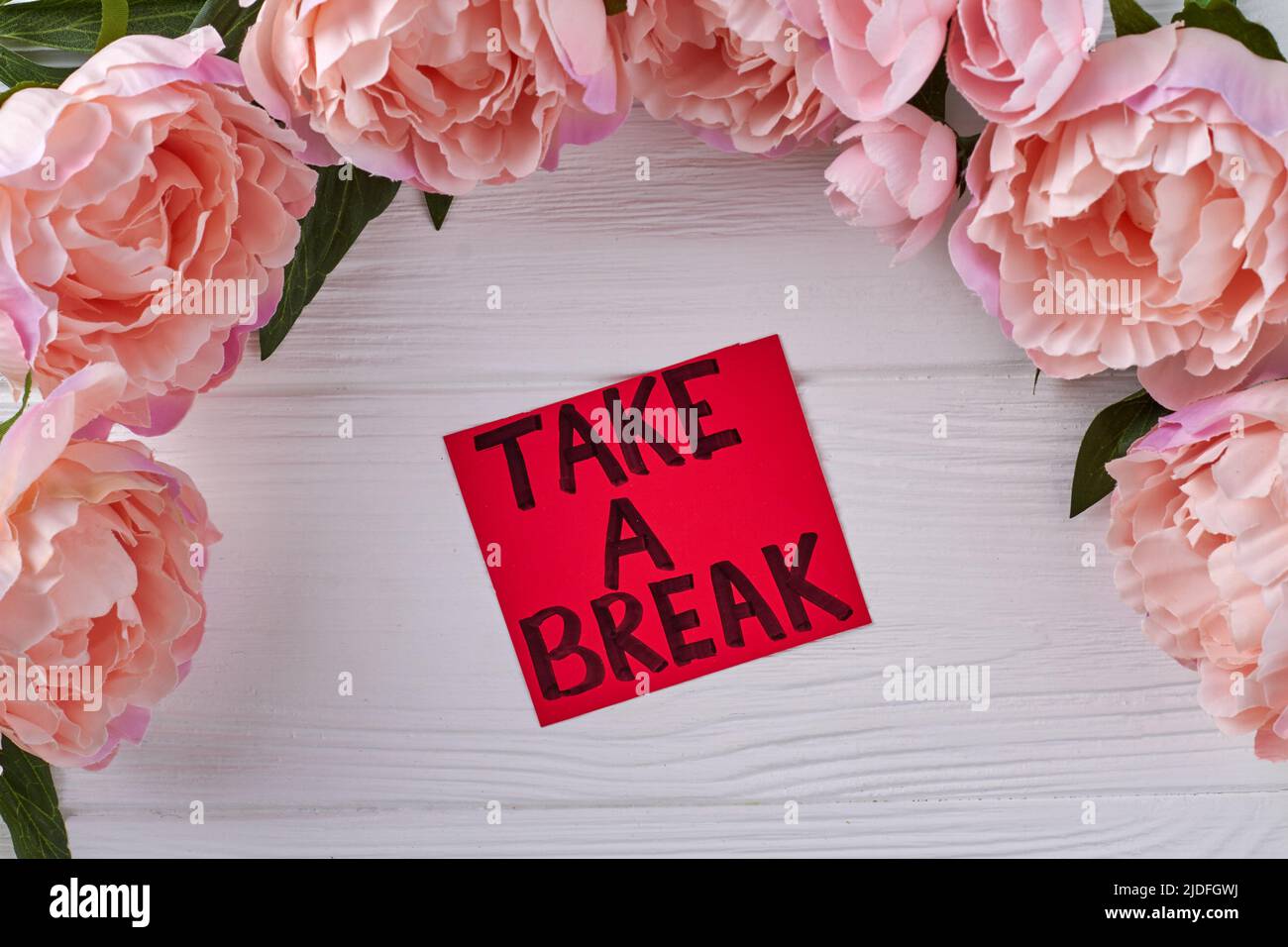 Red paper with take a break handwriting on white desk. Frame of peonies ...