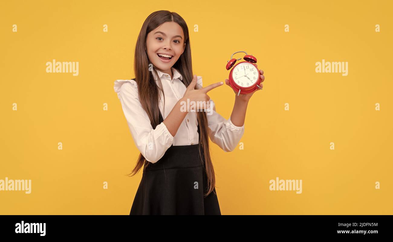 smiling child in school uniform point finger on alarm clock showing ...