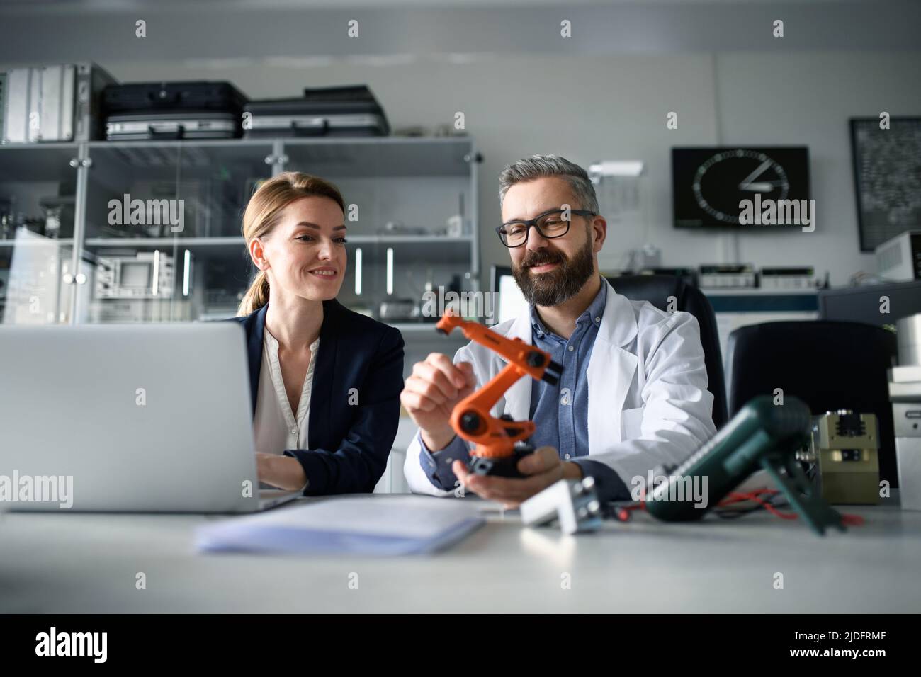 Robotics engineers working on laptop and desinging modern robotic arm ...