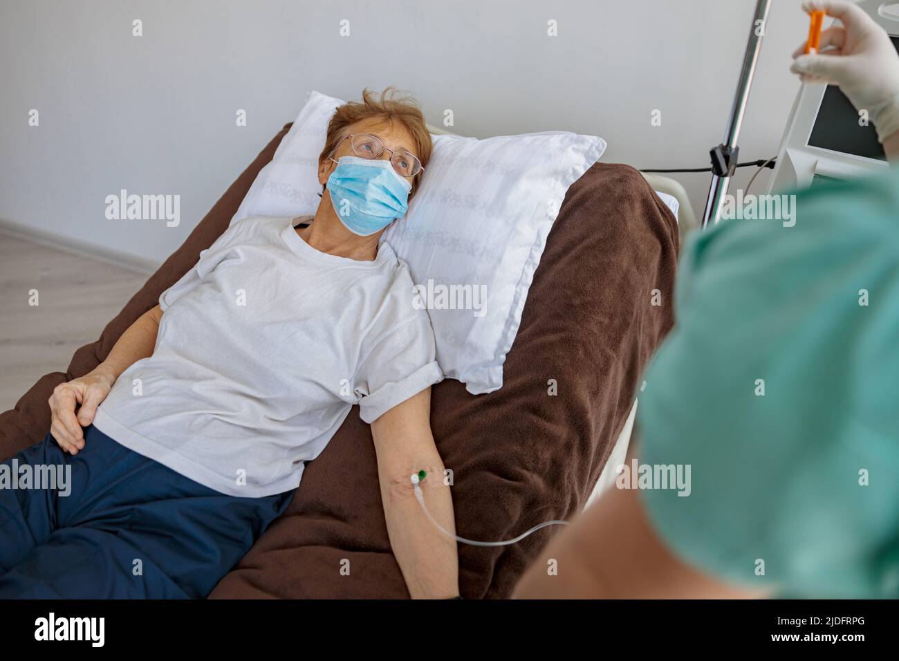 Nurse putting a drip in the arm of her patient in mask during covid-19 ...
