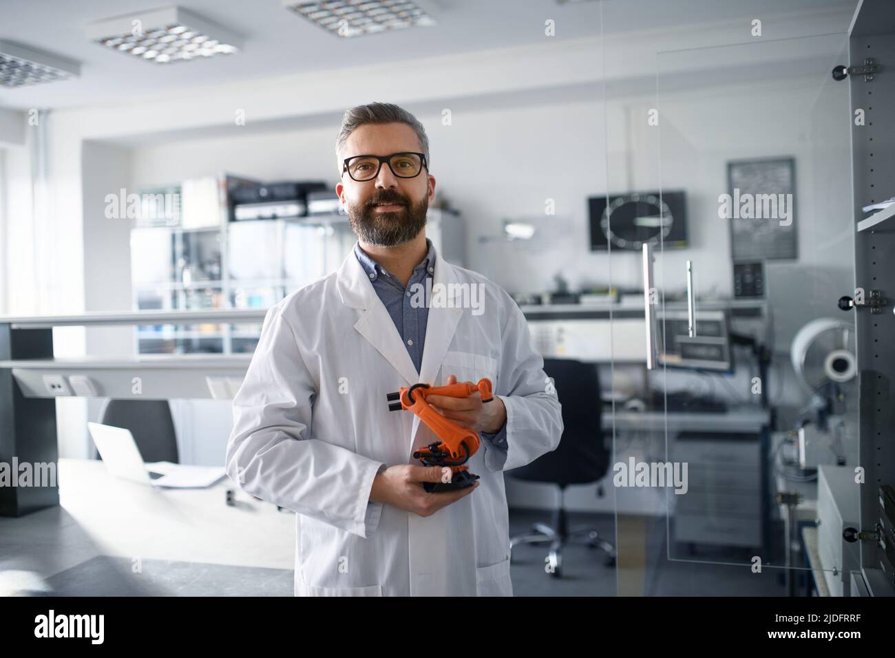 Robotics engineer holding modern robotic arm, standing and looking at ...