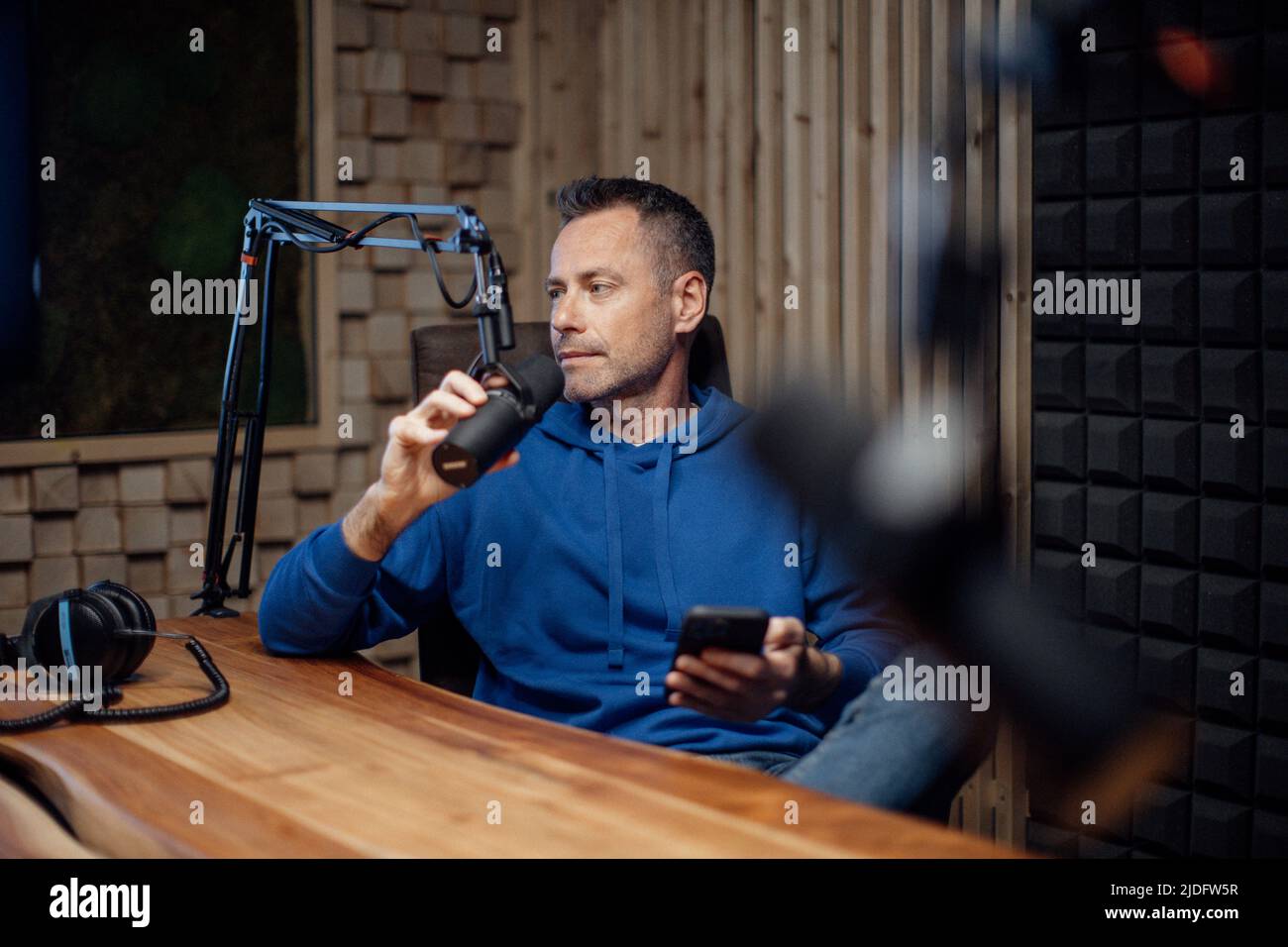 Portrait of mature radio host reading script in cellphone and speaking ...