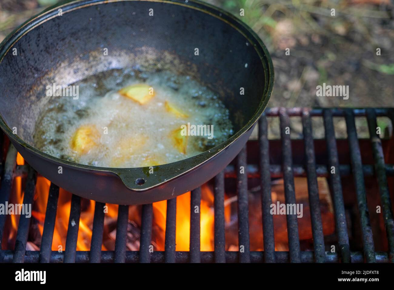 Ruddy tasty potato is frying in cauldron in oil on nature on fire ...