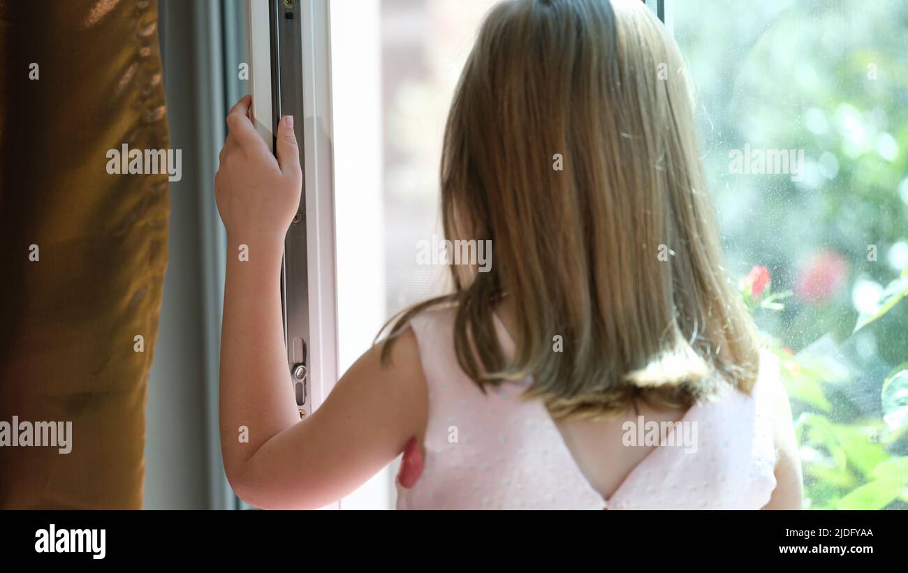 Close-up of little girl standing on windowsill at open window. Danger ...