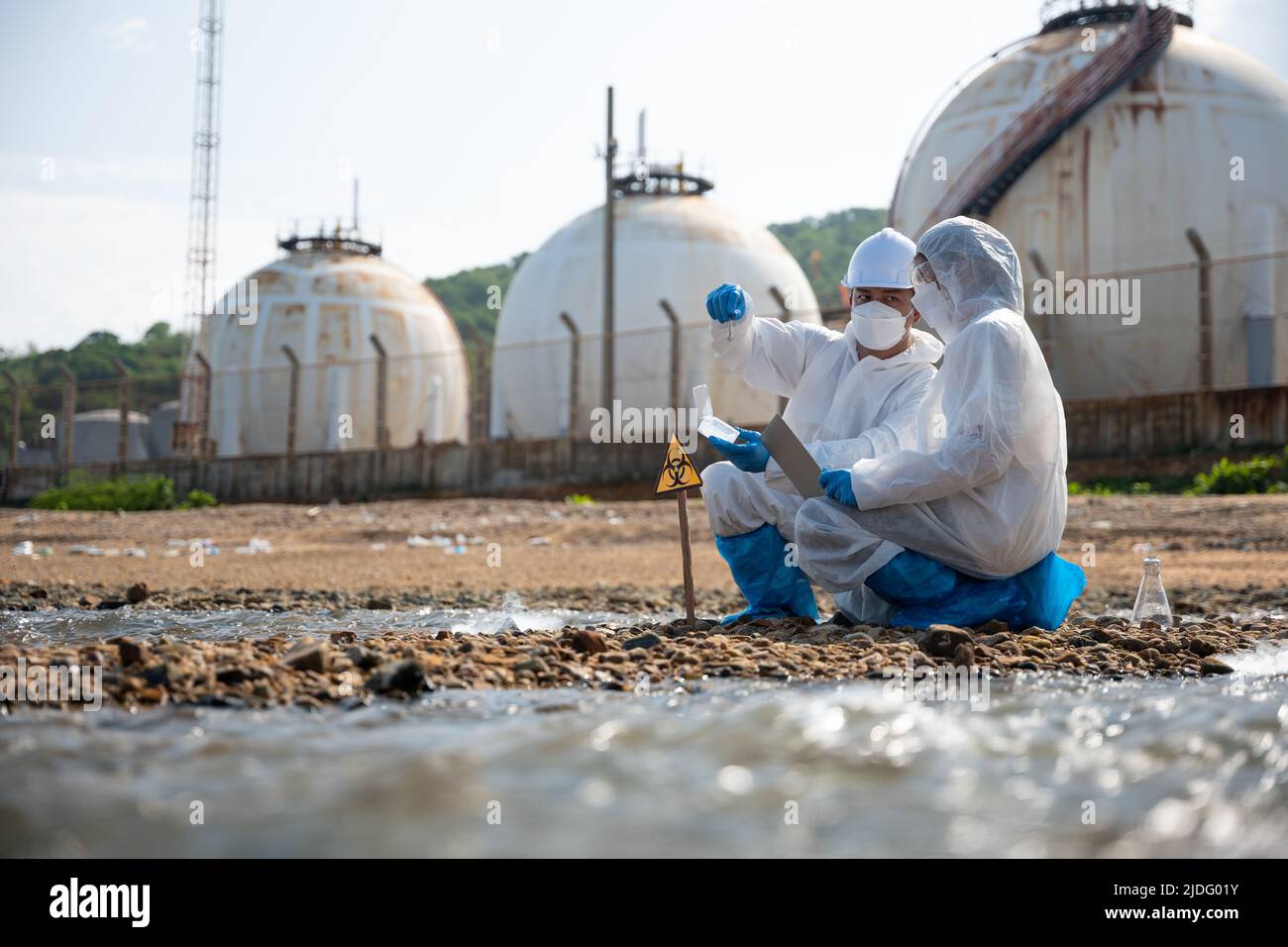 Biologist wear protective suit and mask collects sample of waste water ...
