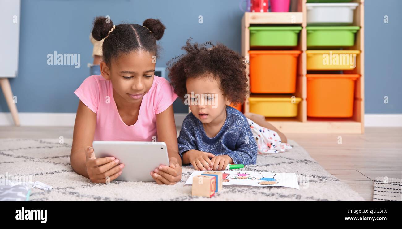 Cute African-American girl with tablet computer watching cartoons at ...