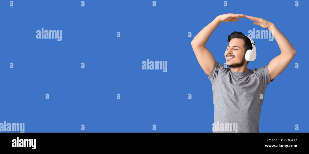 Handsome young man listening to music and dancing on blue background ...