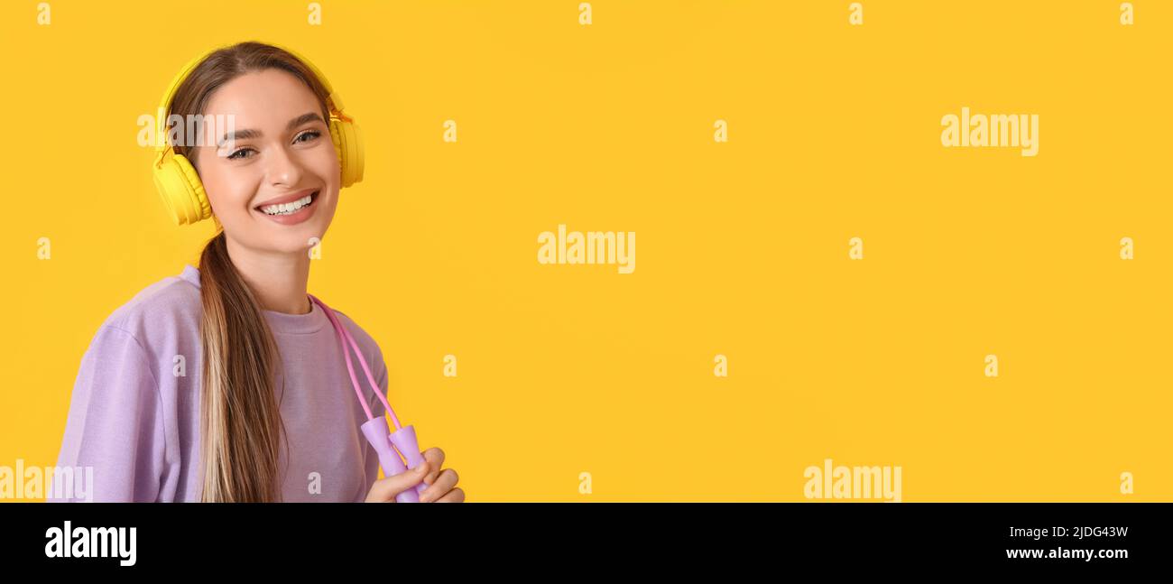 Sporty young woman with jumping rope listening to music on yellow ...