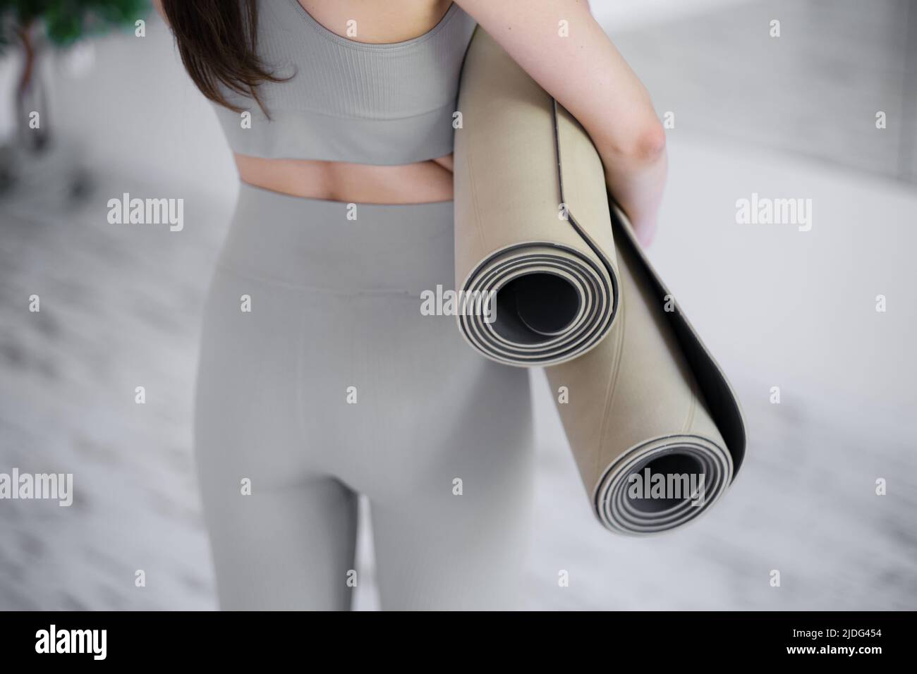 Young beautiful woman holding yoga mats while standing in a light ...